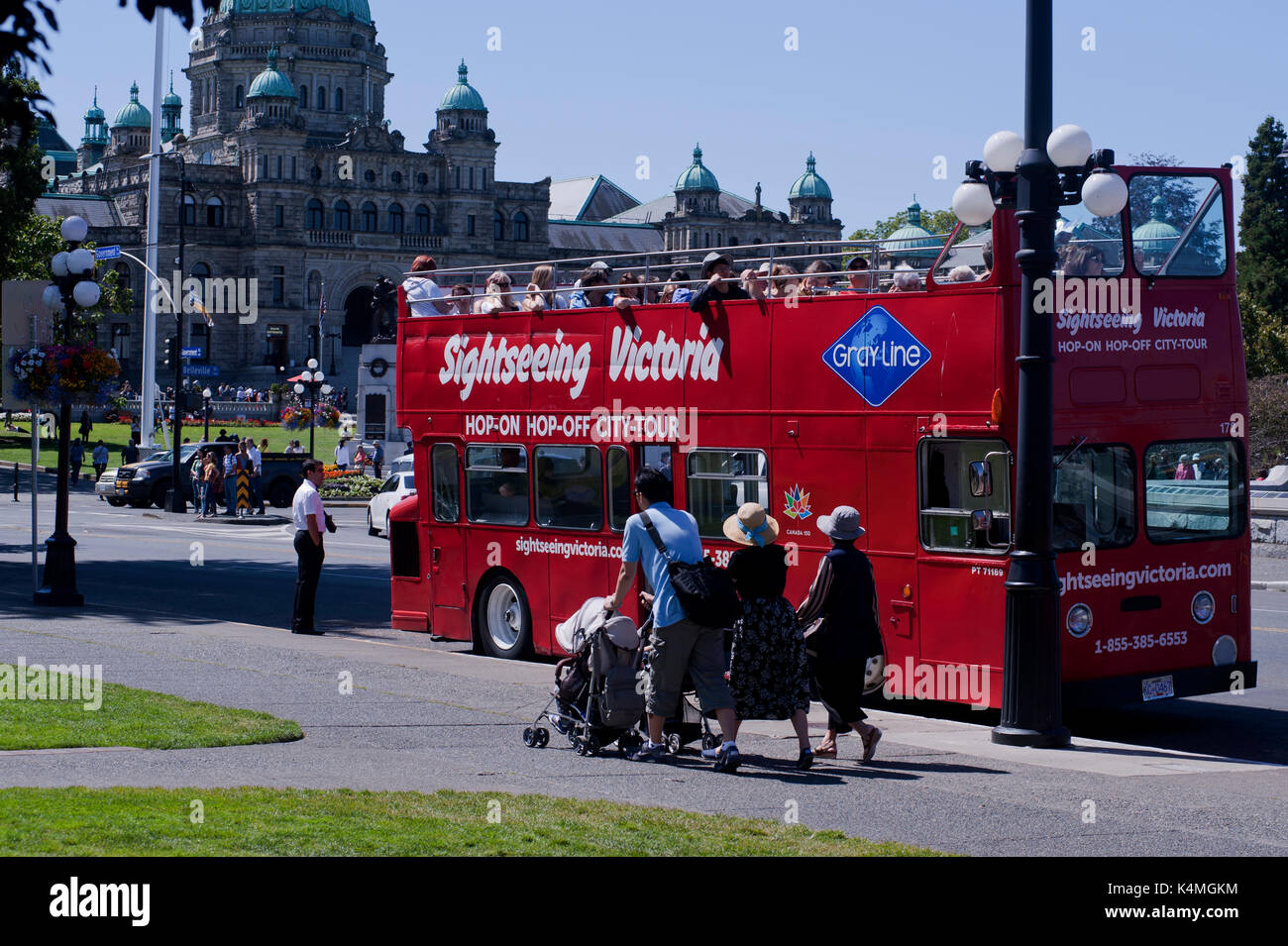 People walk past double-decker tour bus in Victoria with Legislature ...