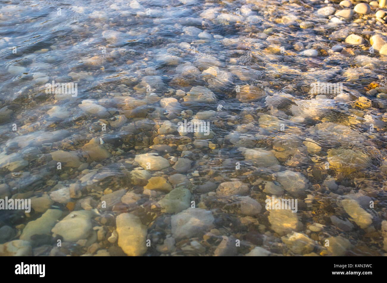 sea pebble beach with multicoloured stones, transparent waves with foam ...
