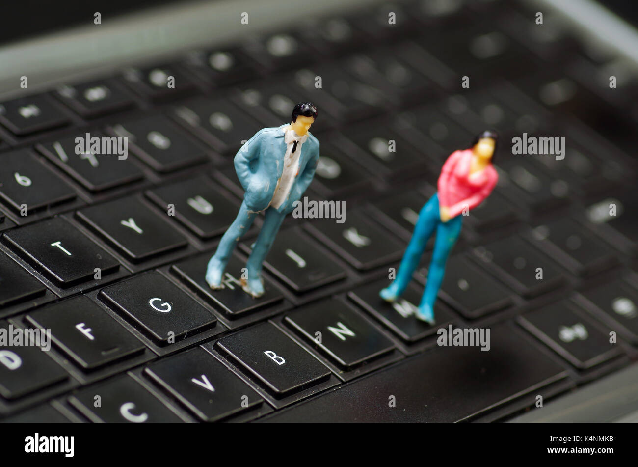 Miniature little people couple over a computer keyboard, in a blurred ...