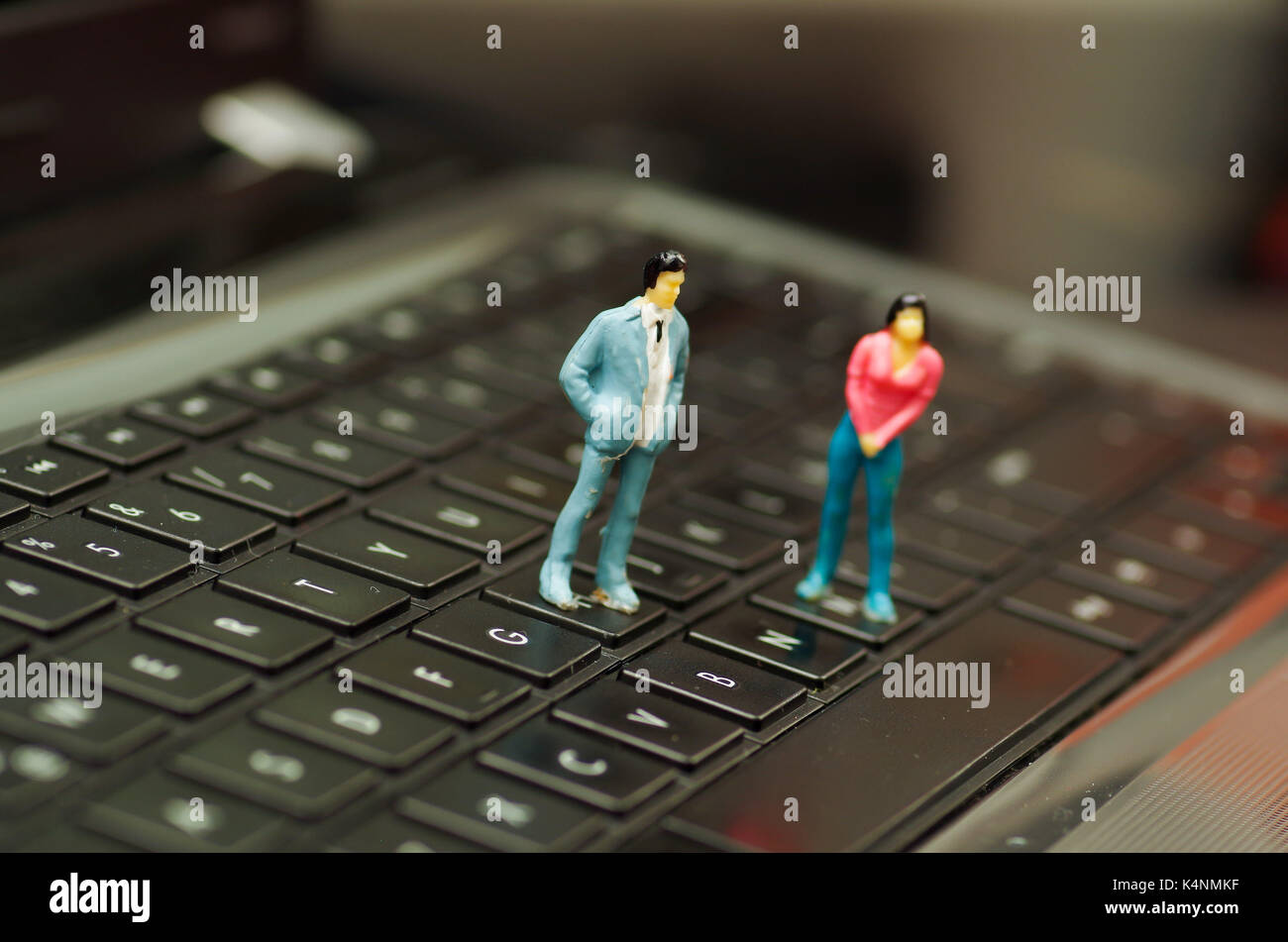 Miniature little people couple over a computer keyboard, in a blurred ...