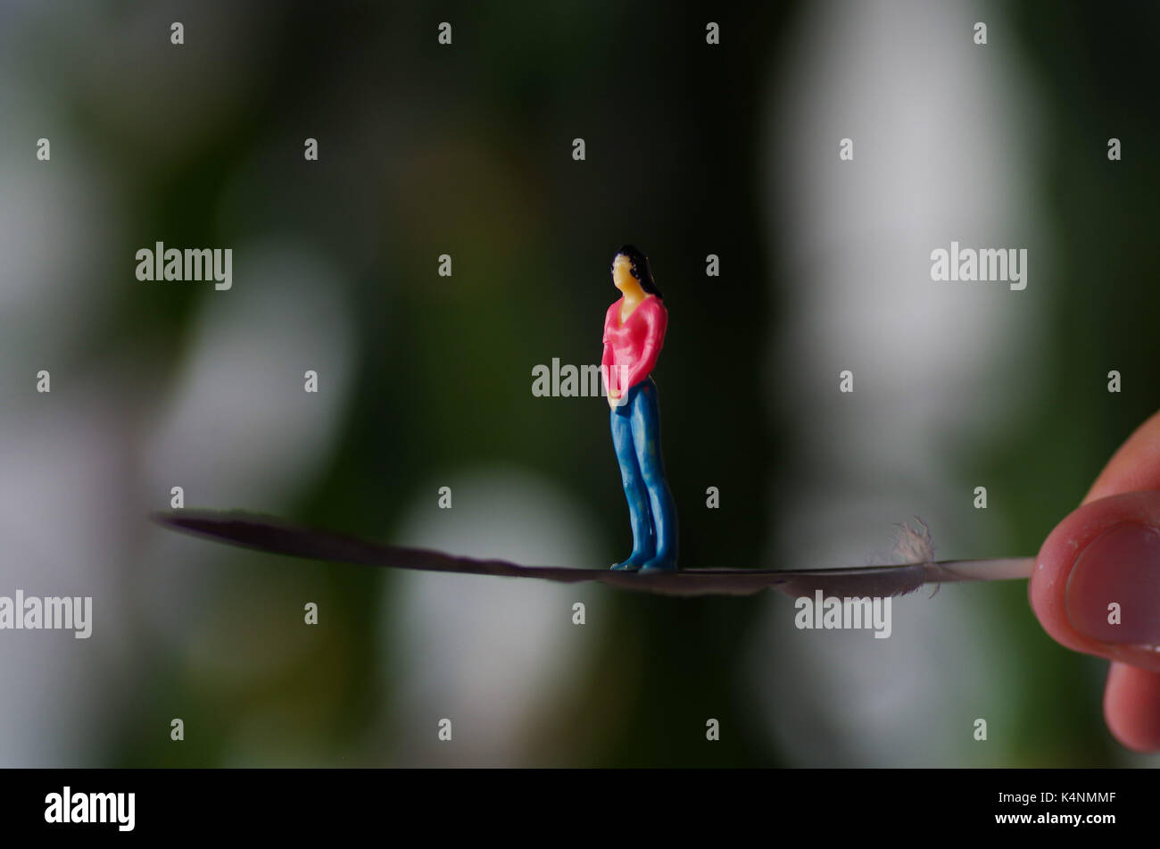 Miniature little people, woman posing over a feather while a hand is ...