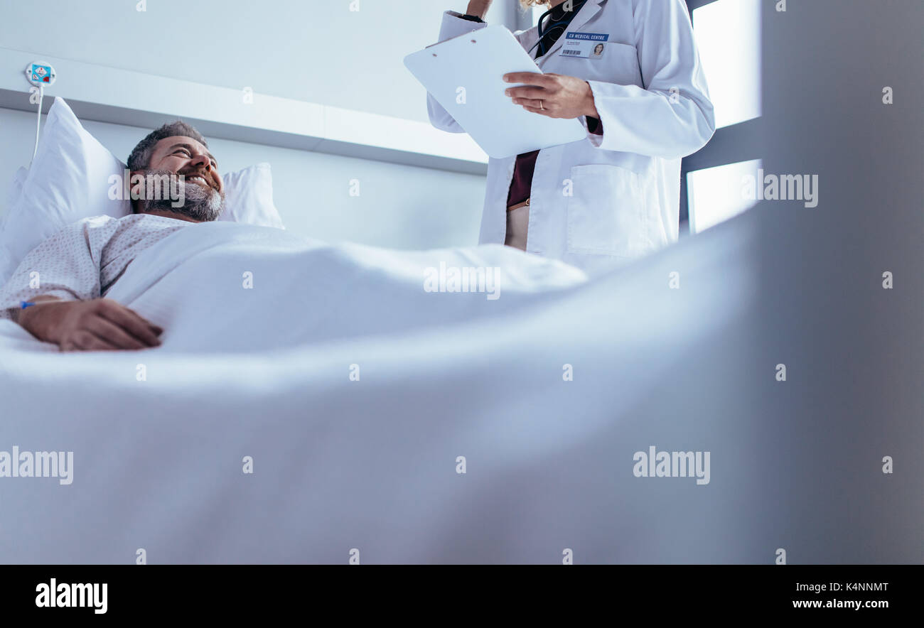 Smiling sick man lying in bed with doctor standing by. Nurse visiting ...