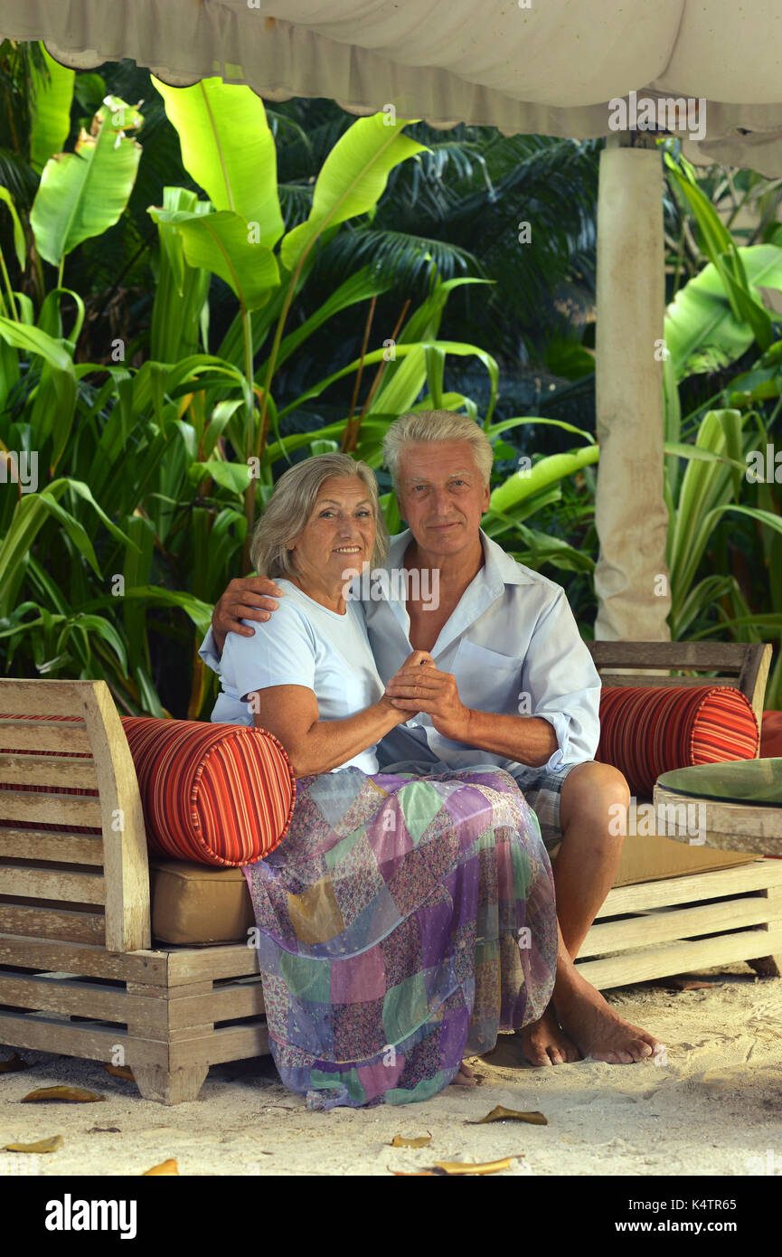 Senior couple sitting on wooden bench with pillow at resort Stock Photo ...