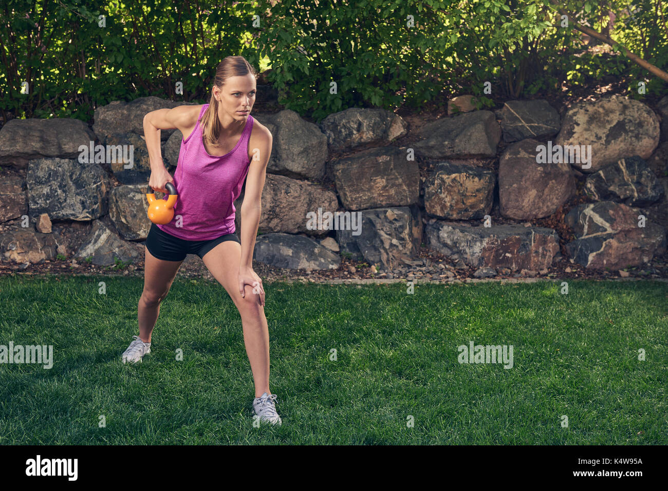 Young woman doing bent leg tricep row with kettlebell on grass in park ...