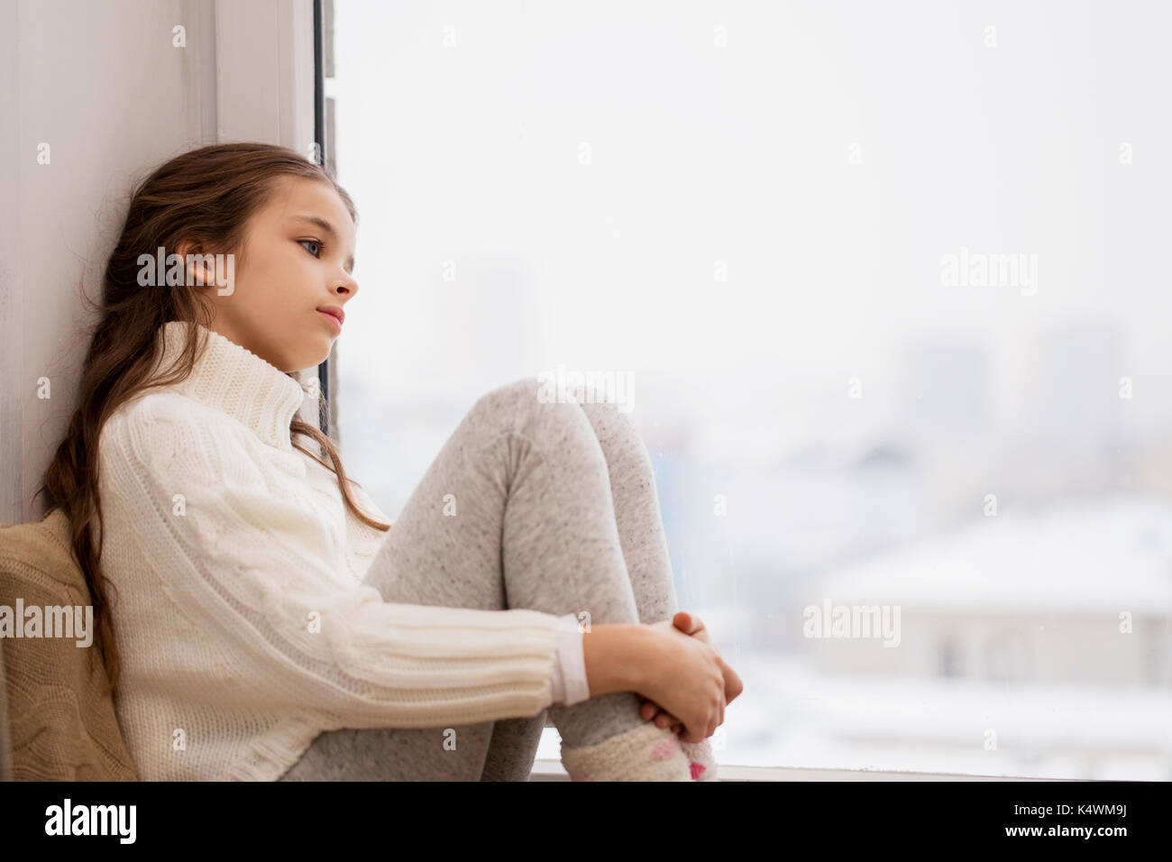 sad girl sitting on sill at home window in winter Stock Photo - Alamy