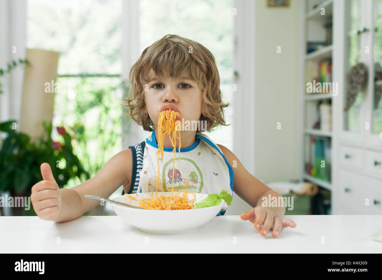 Portrait of a cute young boy making a mess while eating pasta for lunch ...