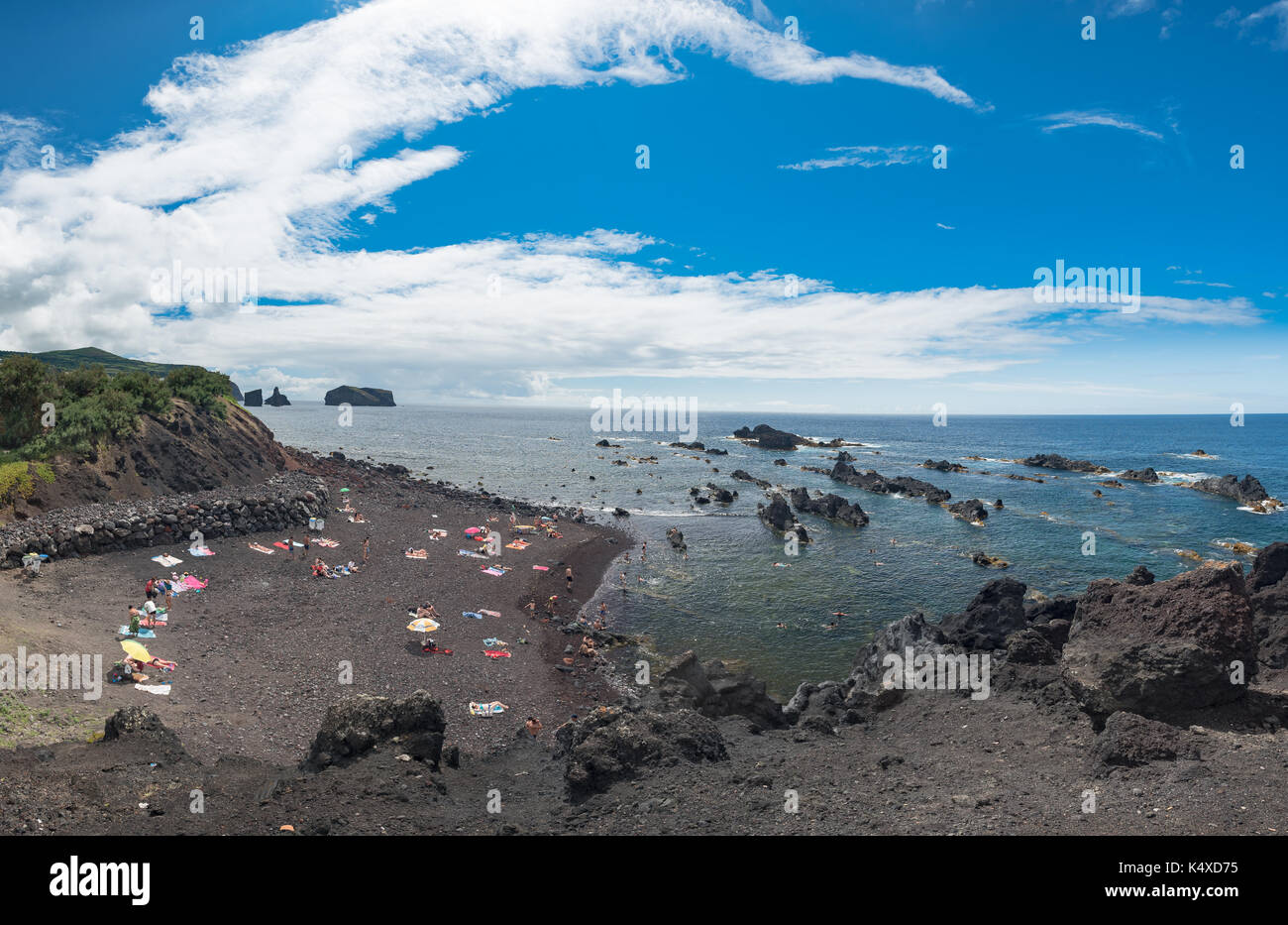 People at the Beach, sunbath on volcanic black sand beach. Rocks at the ...