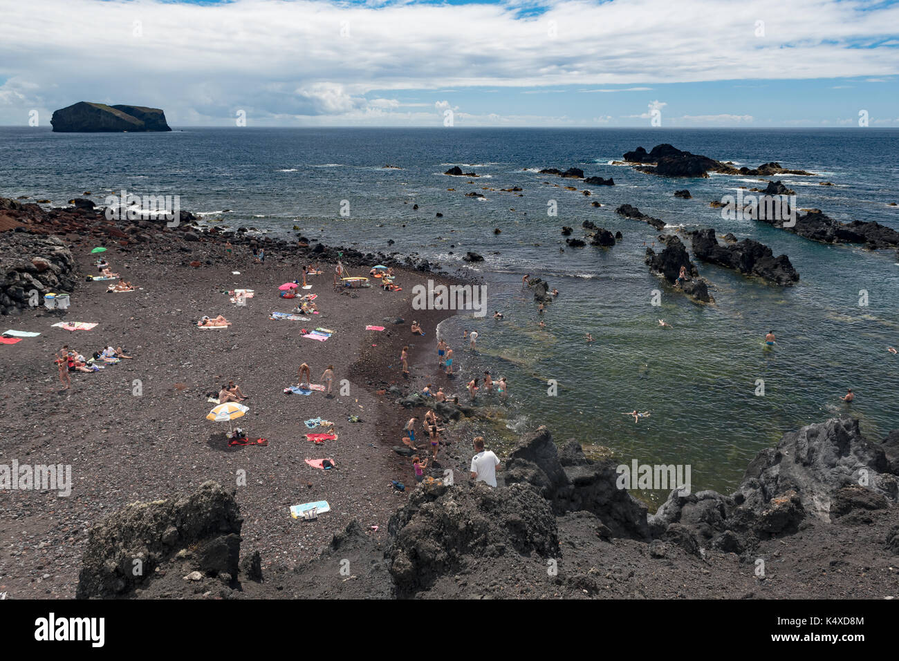 People at the Beach, sunbath on volcanic black sand beach. Rocks at the ...