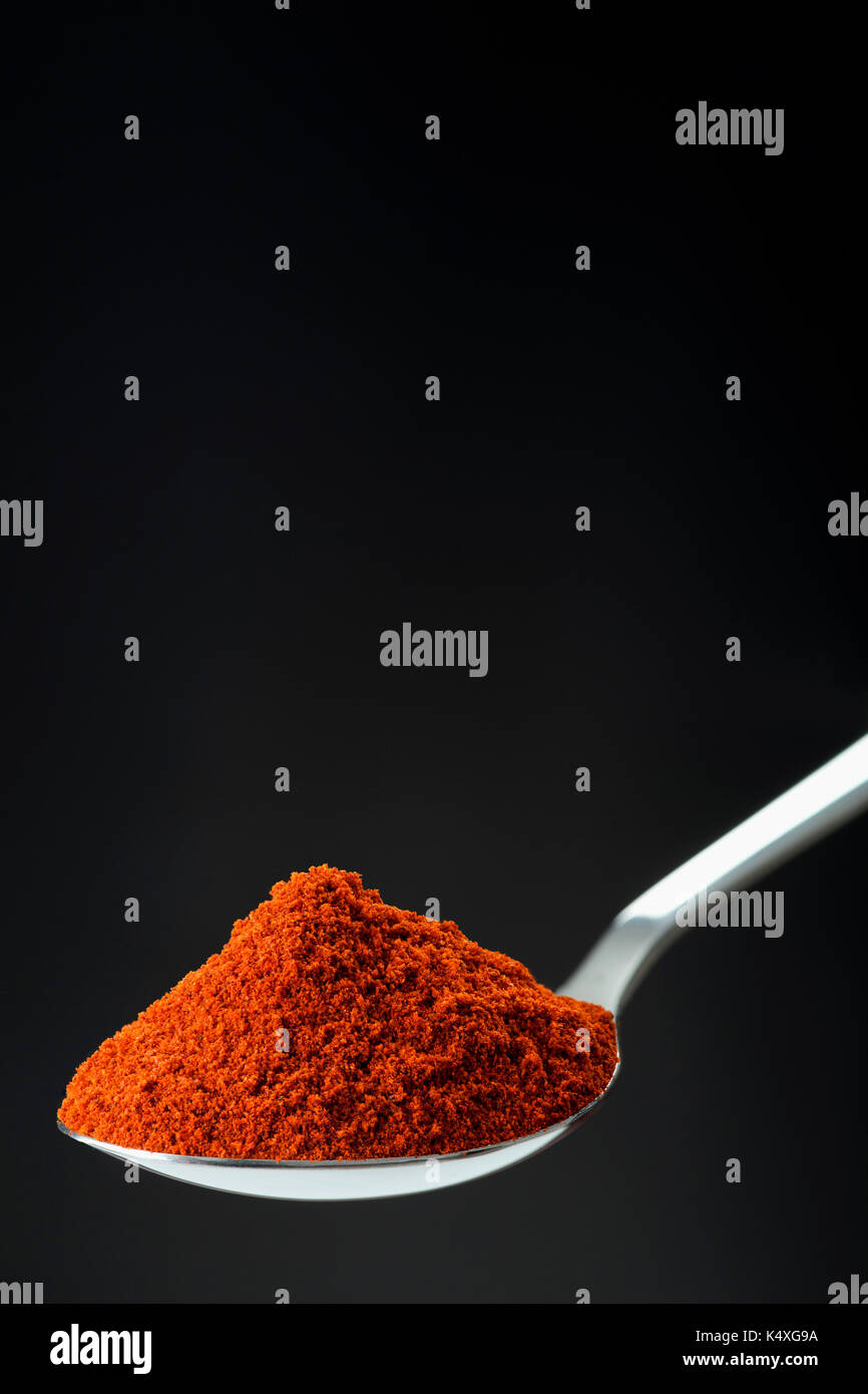 spoon of powder red chili pepper on black background with empty place ...