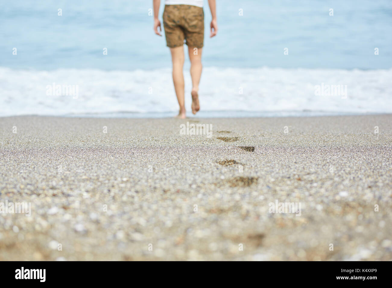 Cropped portrait of man walking on beach leaving footsteps on sand ...