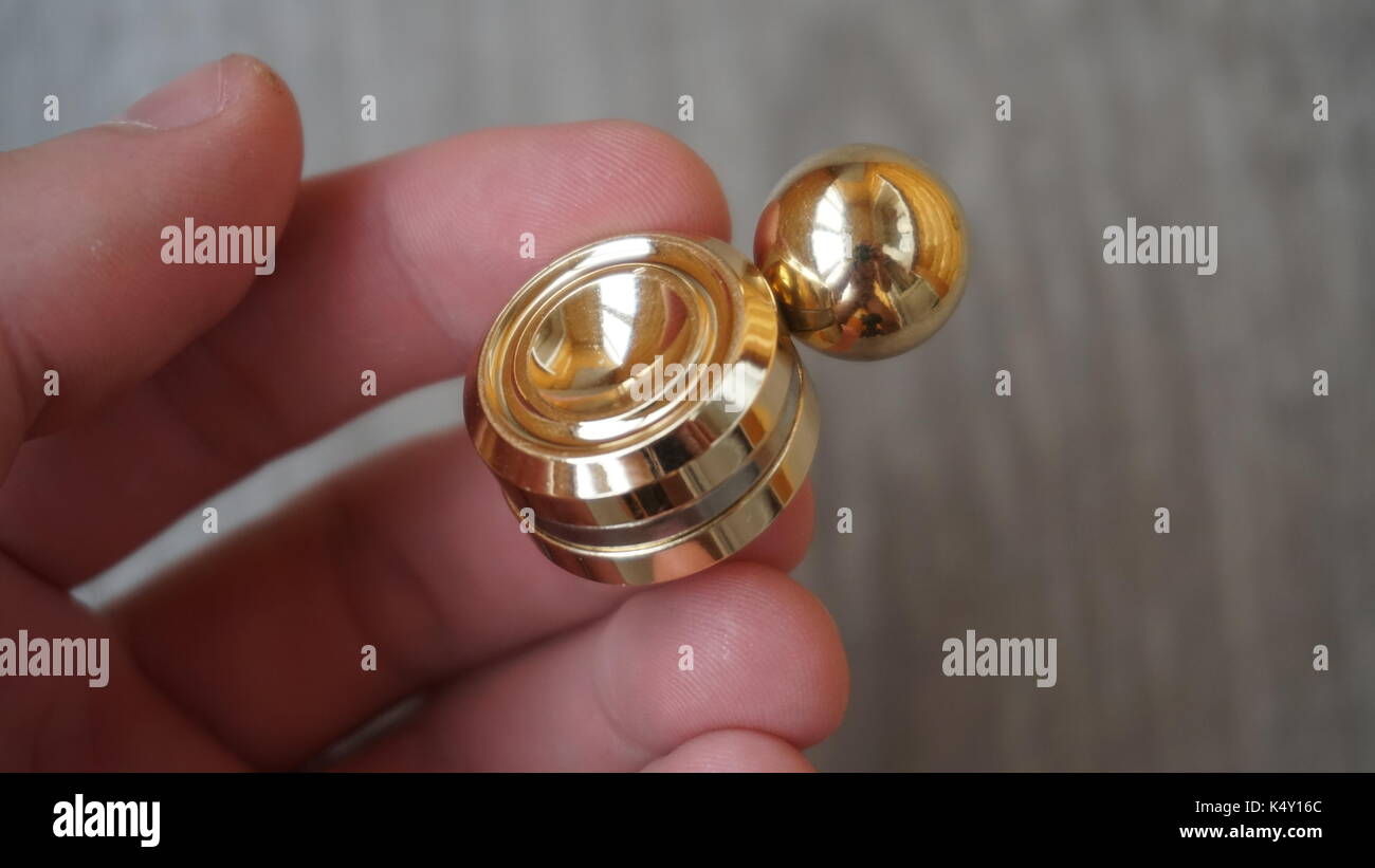 new gold fidget Orbiter,spinning in the hand of a young man on gray ...