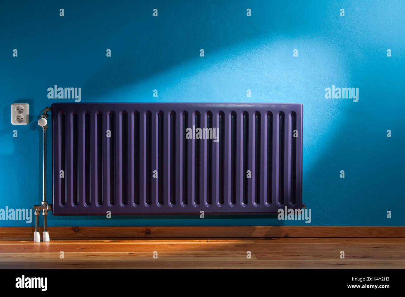 Purple central heating radiator and a blue wall with power point in the ...