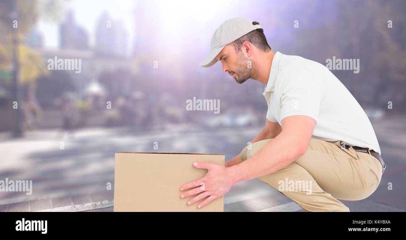 Digital composite of Delivery man picking up box against blurry street ...