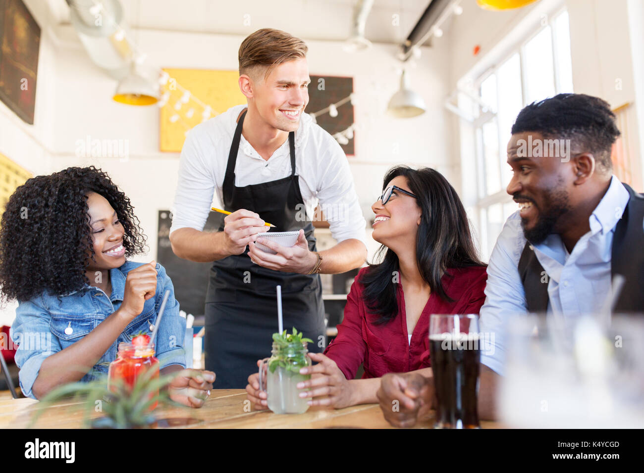 waiter and friends with menu and drinks at bar Stock Photo - Alamy