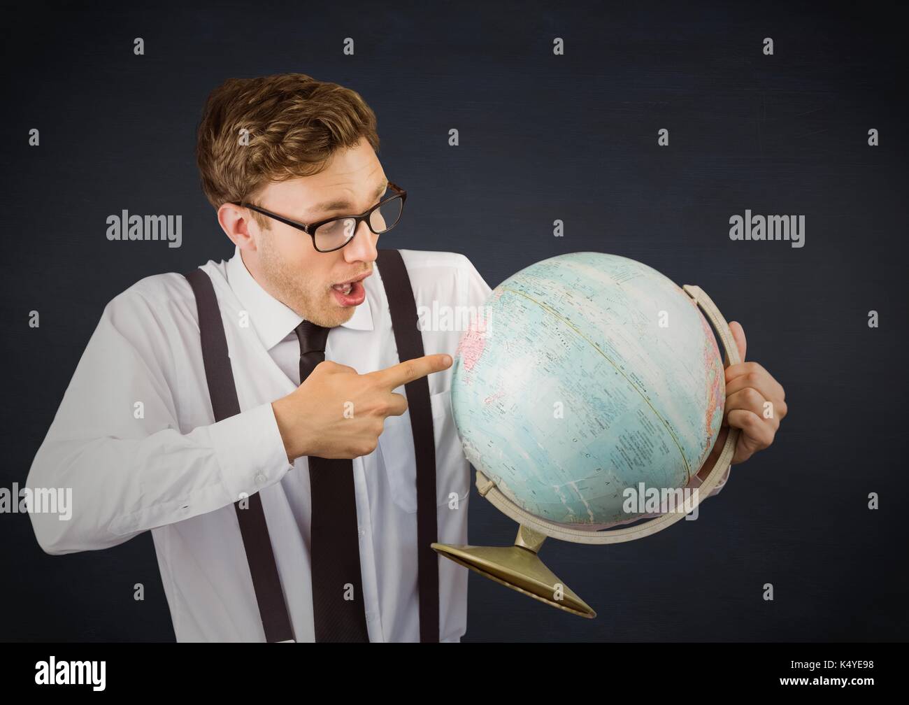 Digital composite of Nerd man pointing at globe against navy chalkboard ...