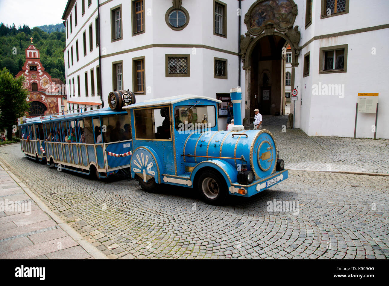 The tourist train in Fussen, Bavaria, Germany passes St Mang's Basilica ...