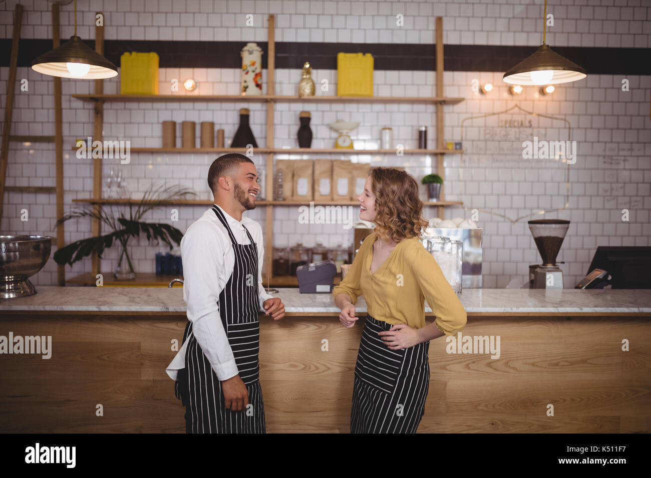 Smiling young wait staff standing at counter against shelf in coffee ...