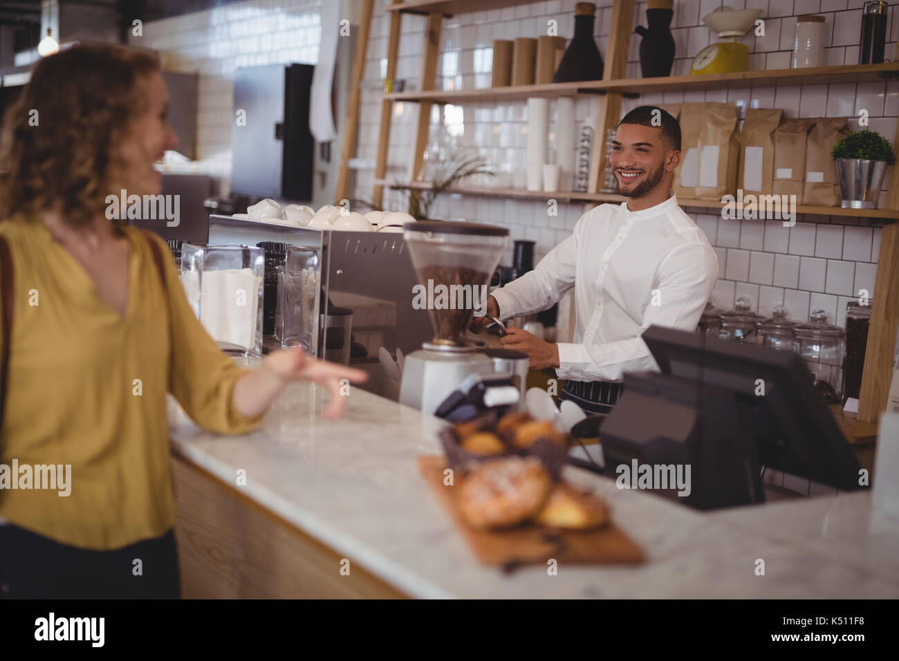 Smiling waiter looking at female customer standing at counter in coffee ...