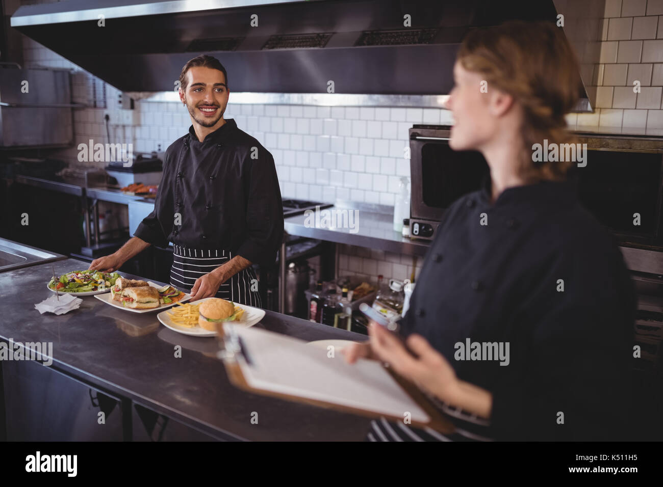 Young waiter preparing food while looking at waitress in coffee shop ...