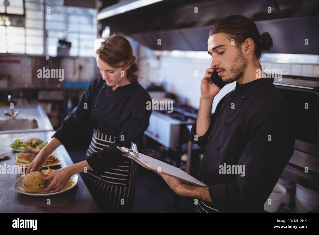 Young waiter talking on smartphone while waitress preparing food in ...