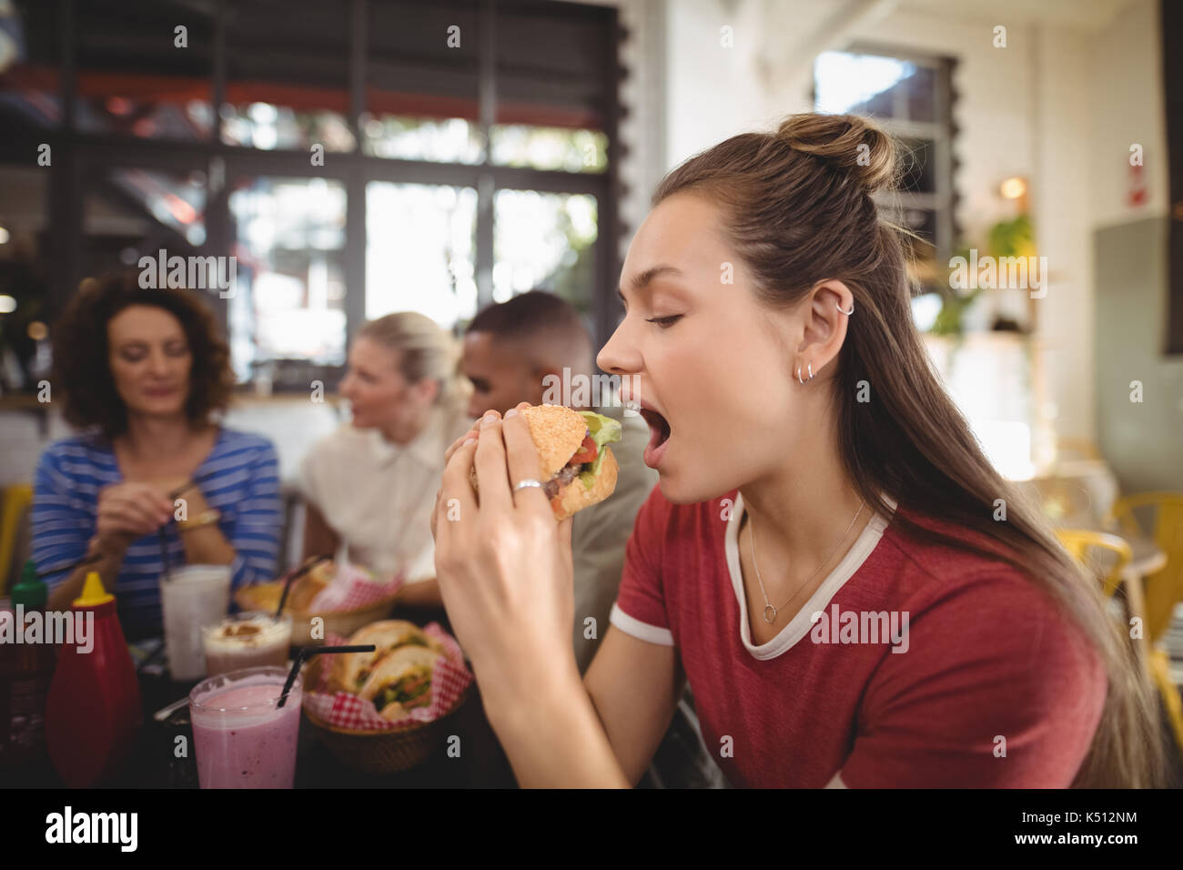 Close up of beautiful young woman eating burger at coffee shop Stock ...