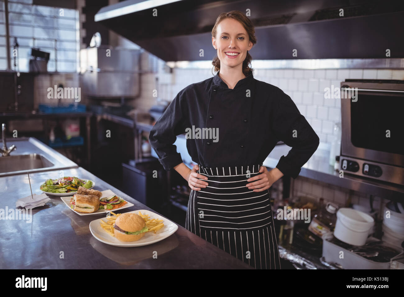 Portrait of smiling young waiter standing with hands on hip by food at ...