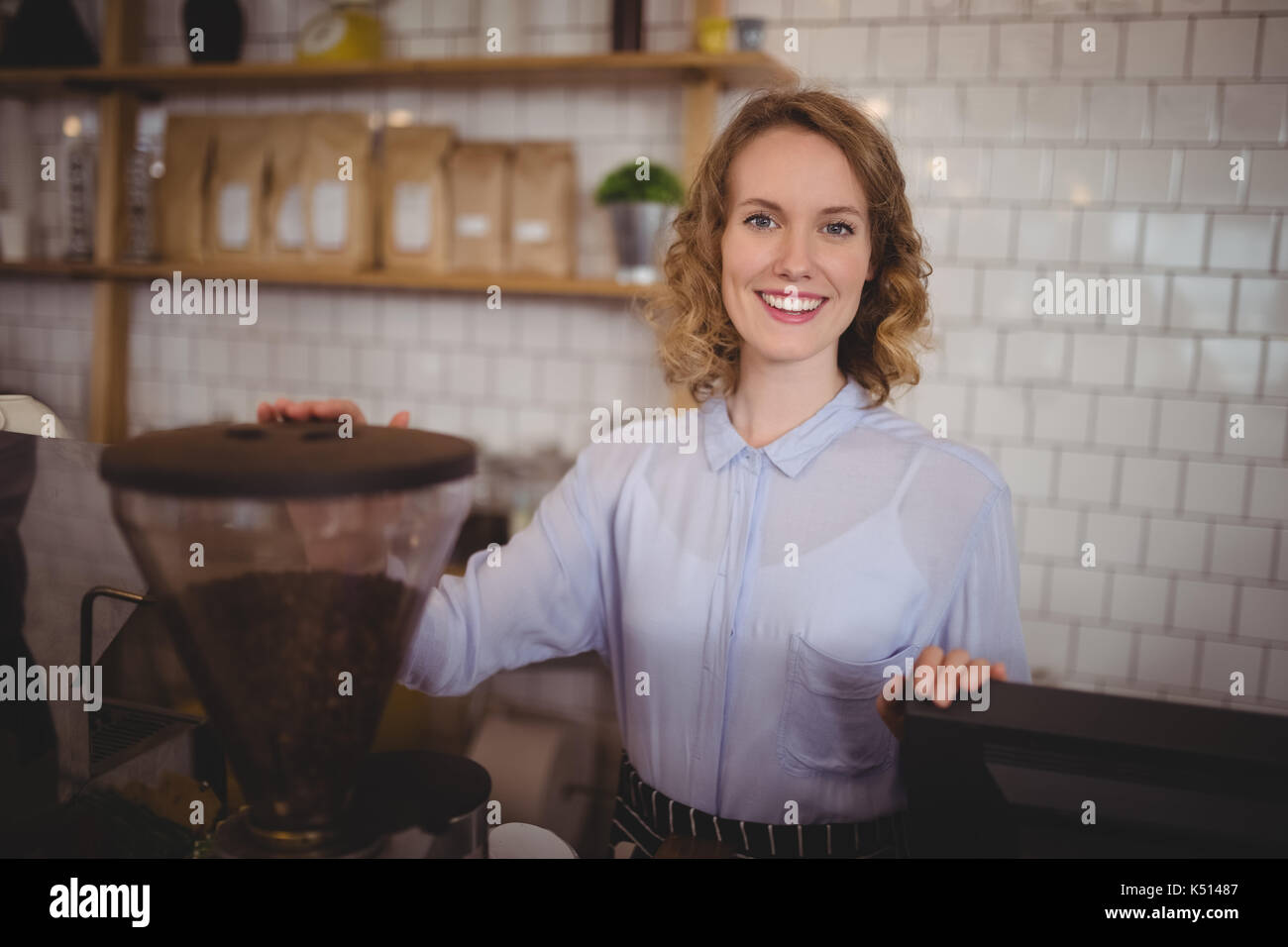 Portrait of smiling young waitress standing by coffee maker at cafe ...