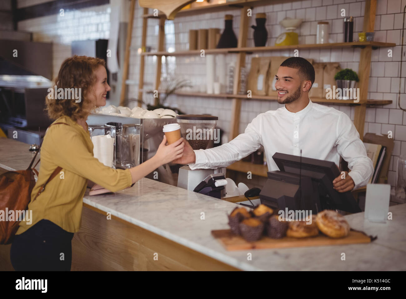 Smiling waiter giving disposable coffee cup to young female customer at ...