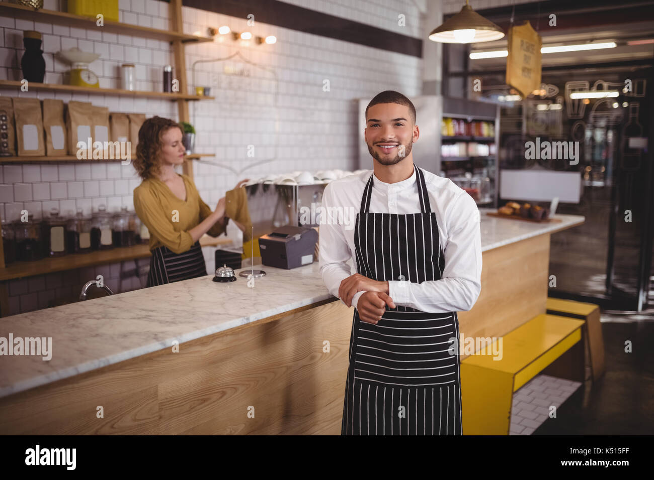 Portrait of waiter standing by counter while waitress working at coffee ...