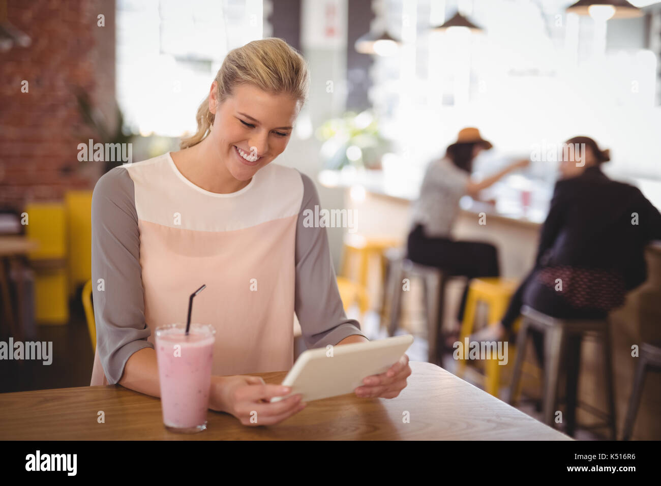 Smiling young blond woman using tablet computer while sitting with ...