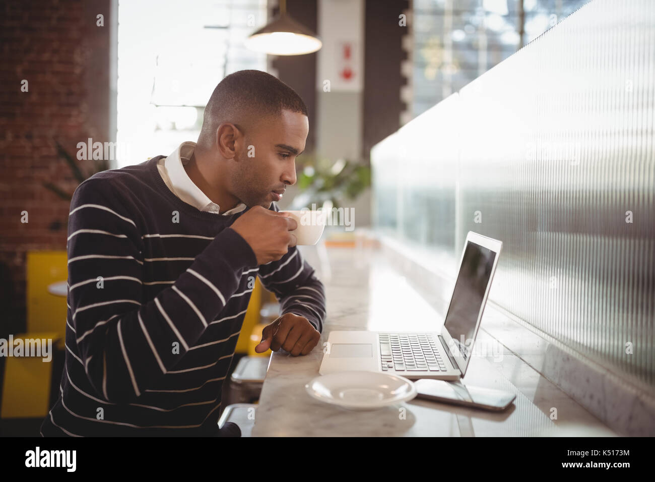 Side view of young man drinking coffee while looking at laptop in cafe ...