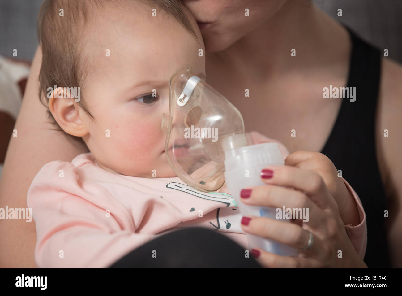 One year old baby girl inhaling from the inhaler, her mother holding ...