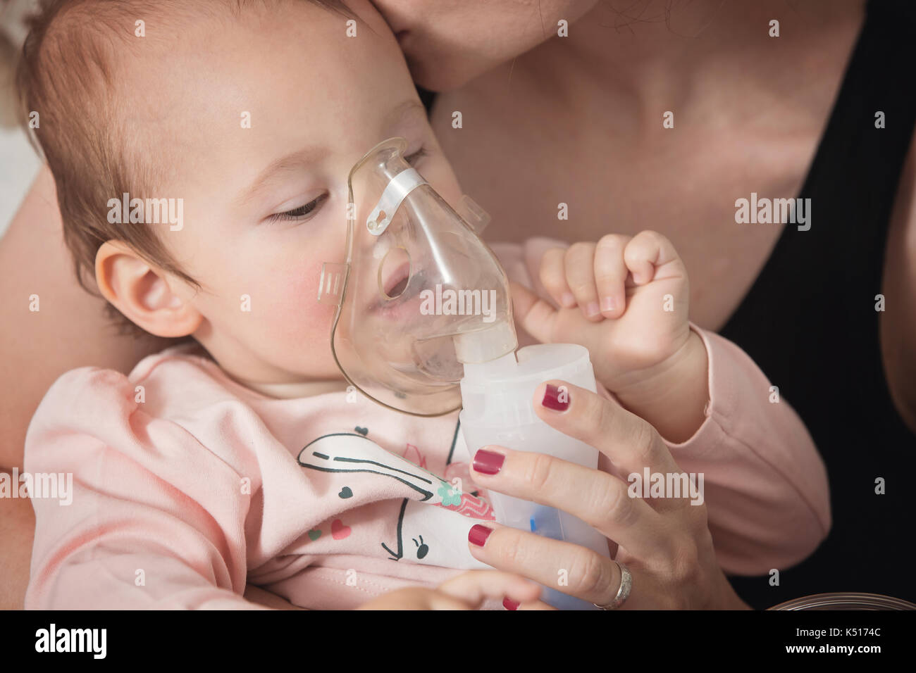 One year old baby girl inhaling from the inhaler, her mother holding ...