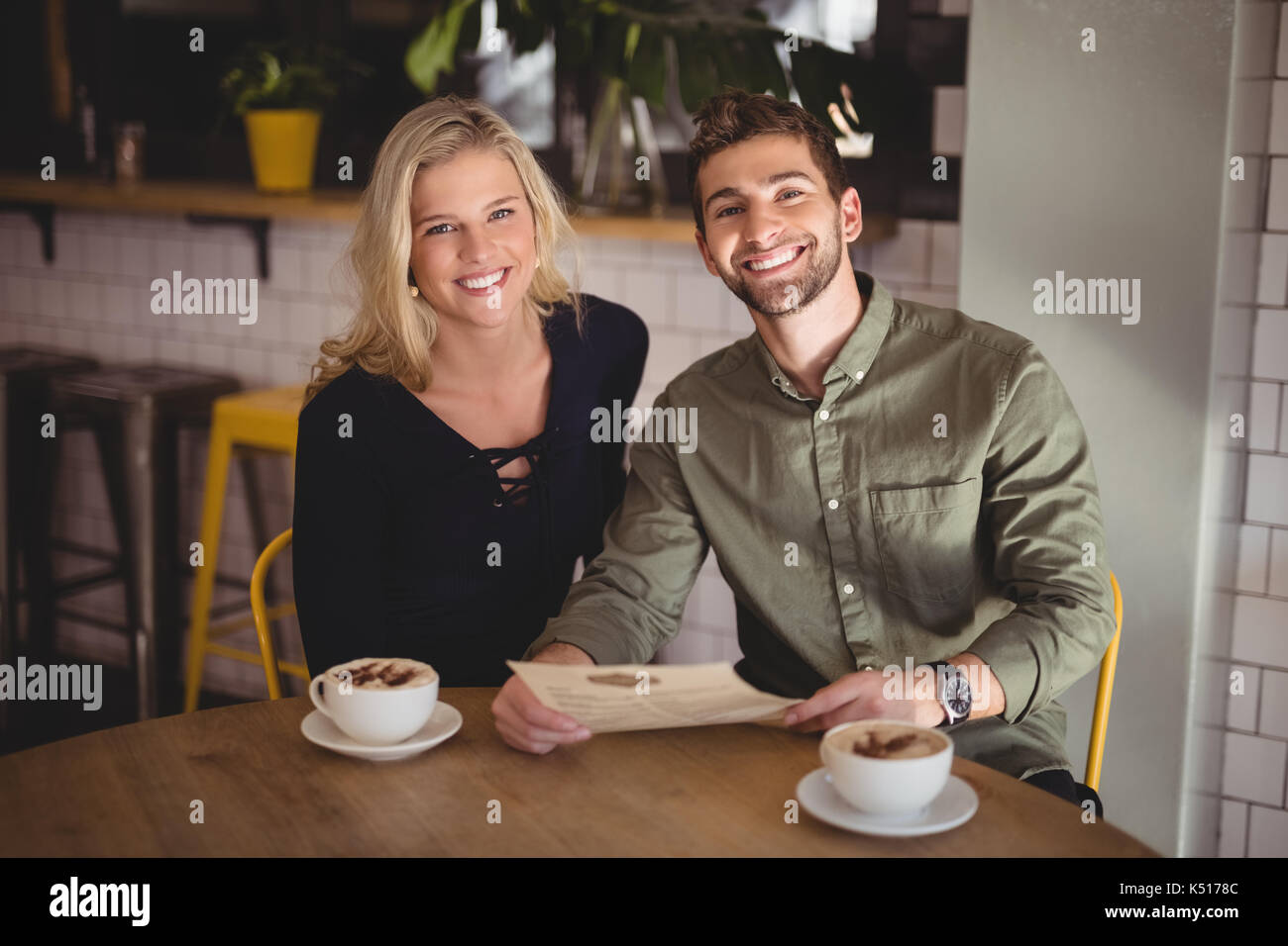 Portrait of smiling young couple sitting with coffee cups and menu at ...