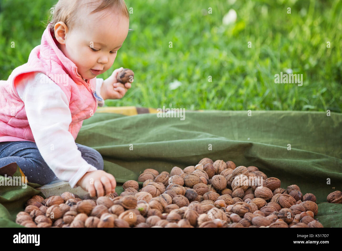 One year old baby sitting on the pile of walnuts and hazelnuts drying ...