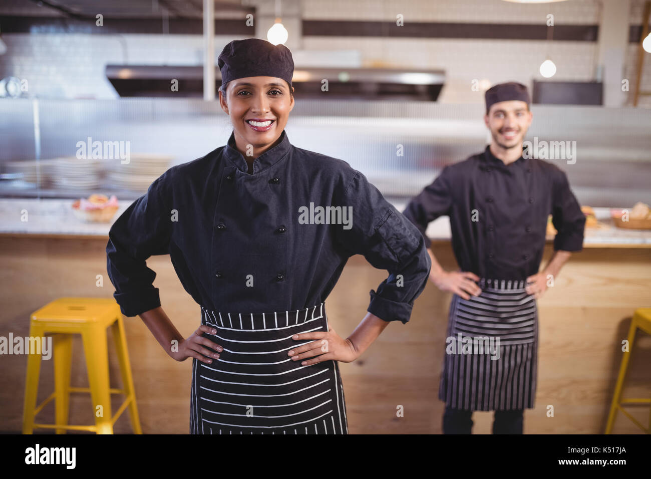 Portrait of smiling young wait staff standing with hands on hip against ...