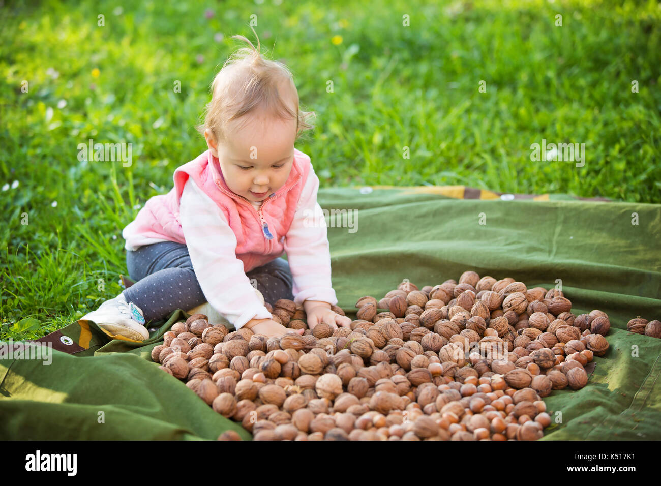 One year old baby sitting on the pile of walnuts and hazelnuts drying ...