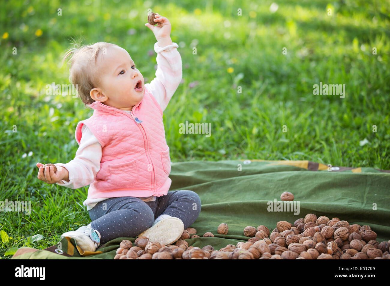One year old baby sitting on the pile of walnuts and hazelnuts drying ...