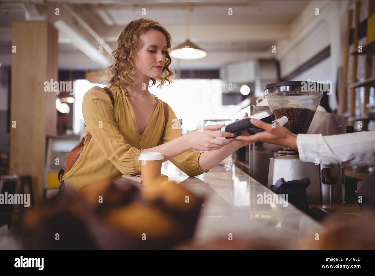 Young female customer paying through card at counter in coffee shop ...