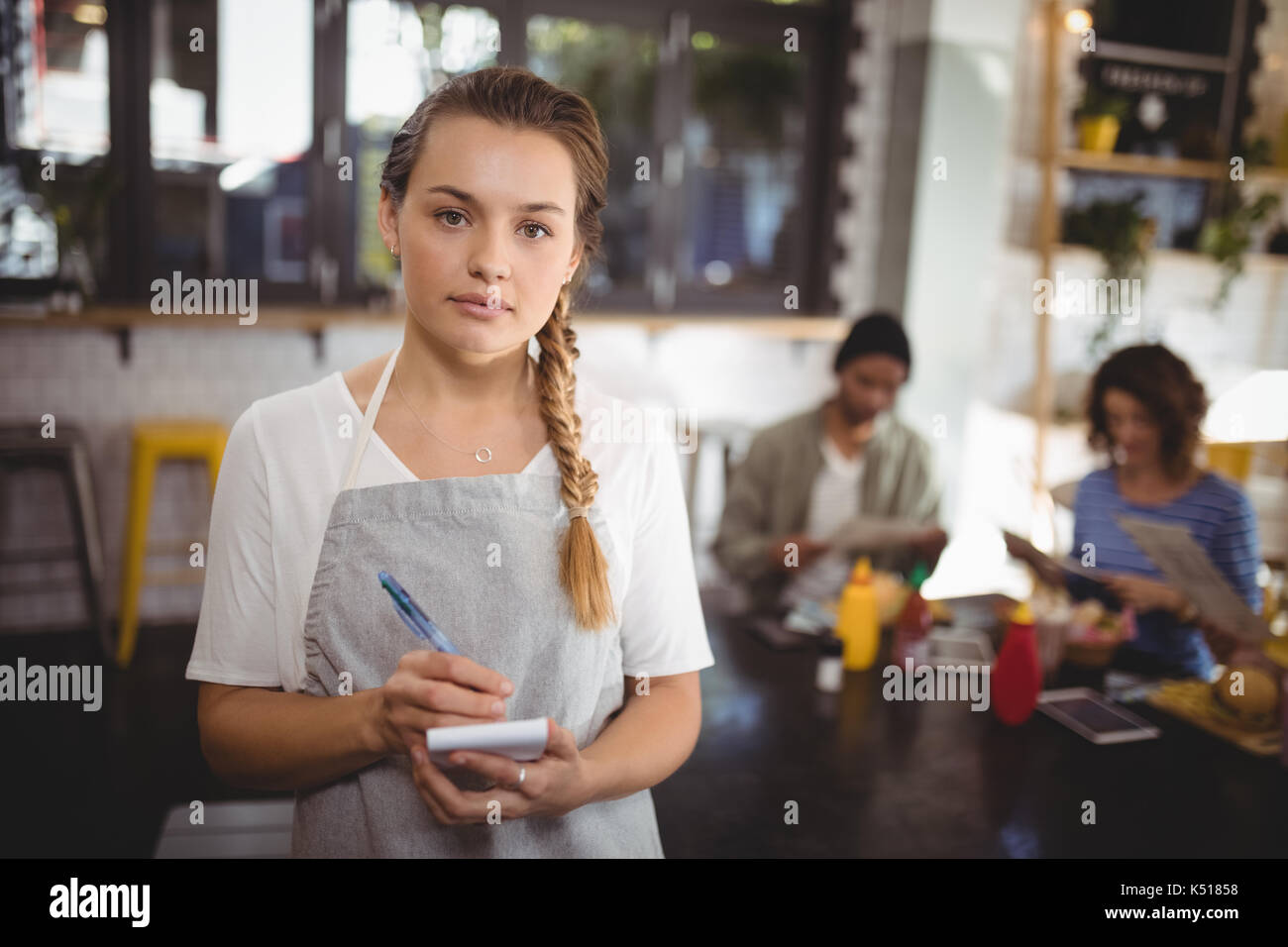 Portrait of confident young waitress standing with notepad at cafe ...