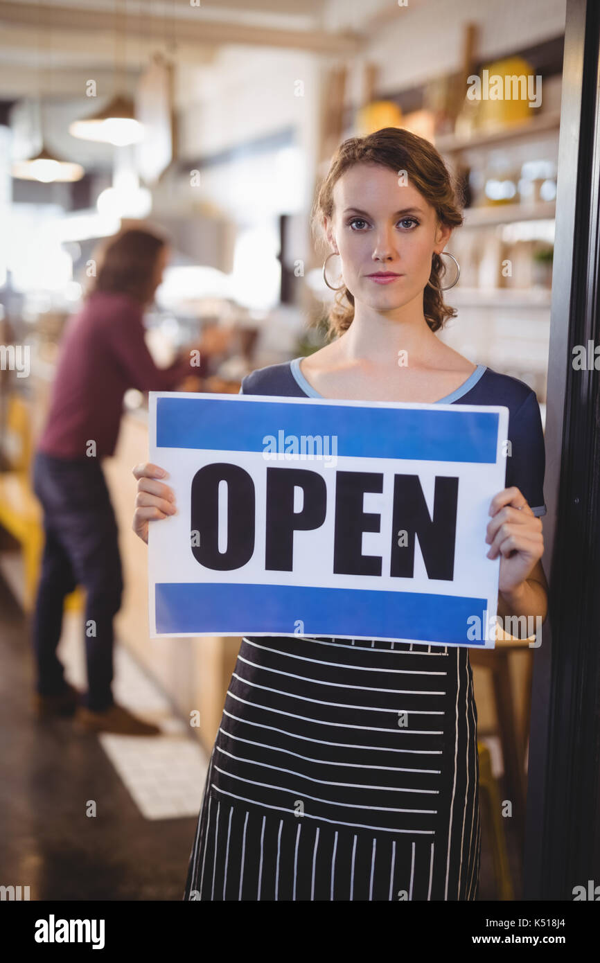 Portrait of confident young waitress holding open sign placard at ...