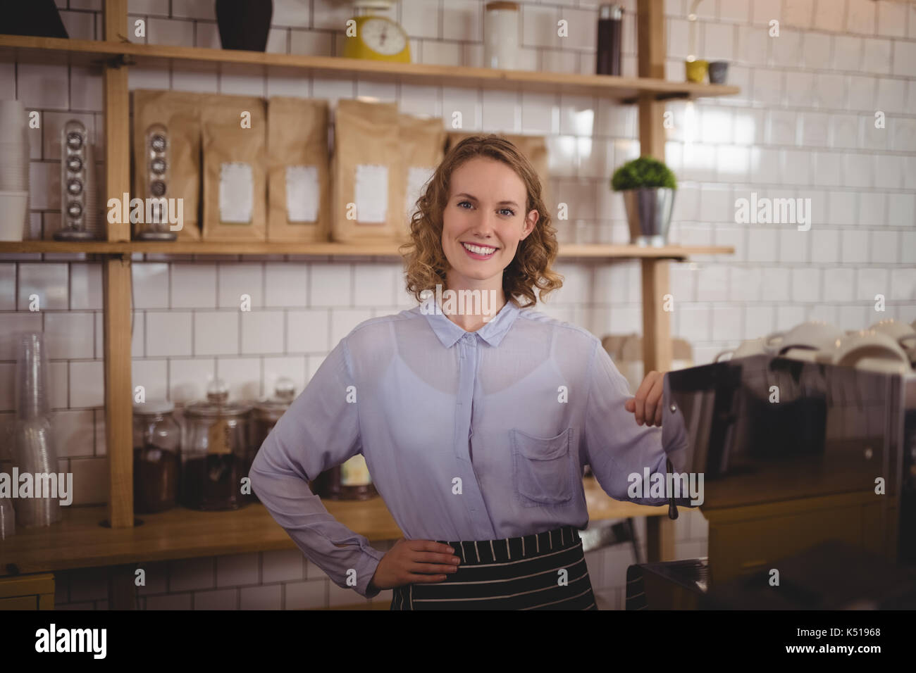 Portrait of confident young waitress standing with hand on hip at ...