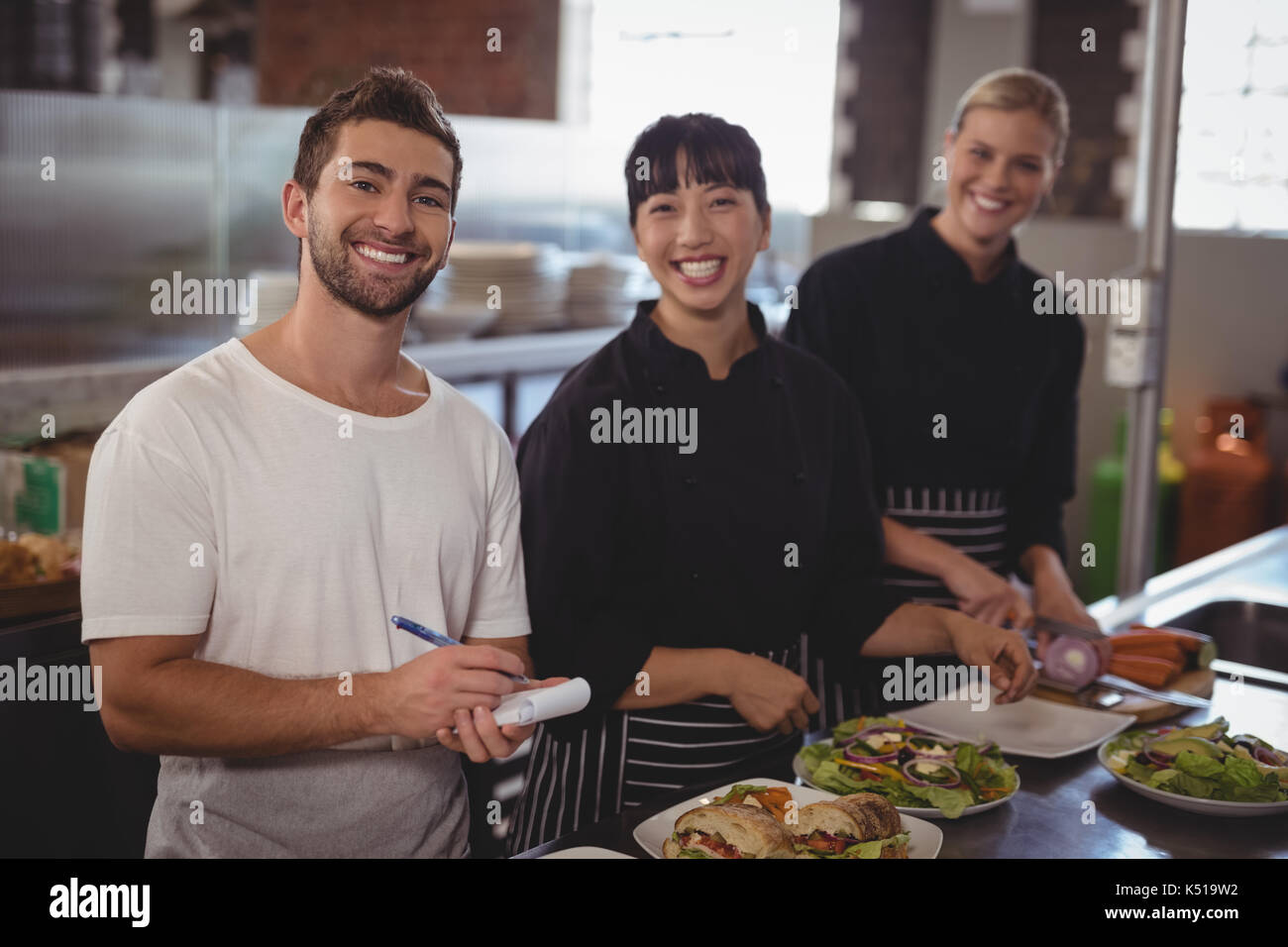 Portrait of waiter with female chefs standing with food in kitchen at ...