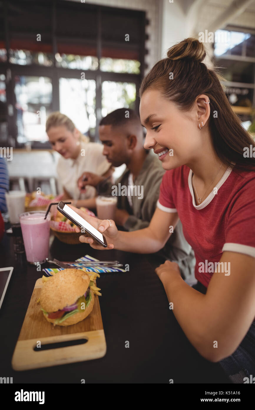 Side view of smiling young woman text messaging while sitting with ...