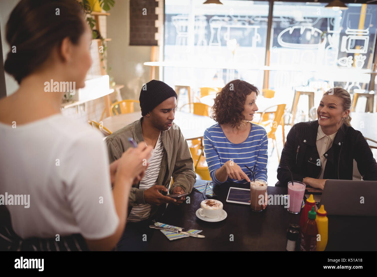 Smiling woman siting with friends ordering food to waitress at cafe ...
