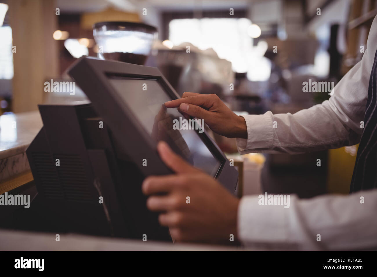 Midsection of waiter touching computer monitor at counter in coffee ...