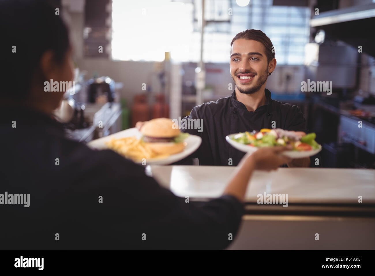 Smiling young waiter giving food to waitress at counter in coffee shop ...