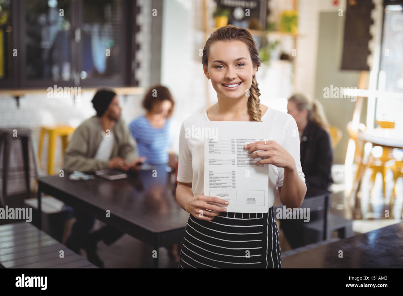 Portrait of smiling young waitress standing with menu card at cafe ...