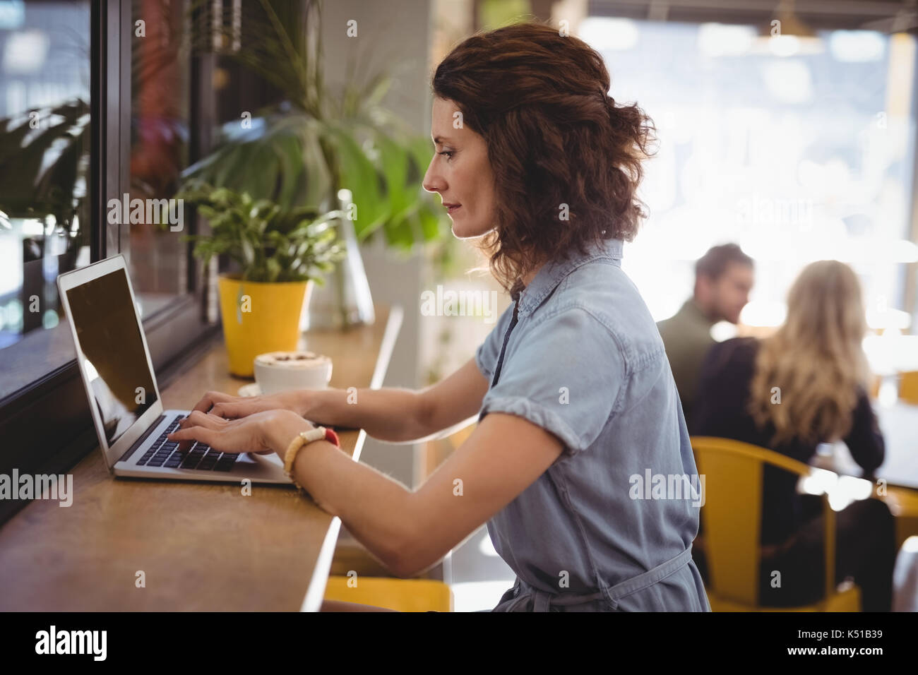 Side view of young woman using laptop while sitting at counter in cafe ...