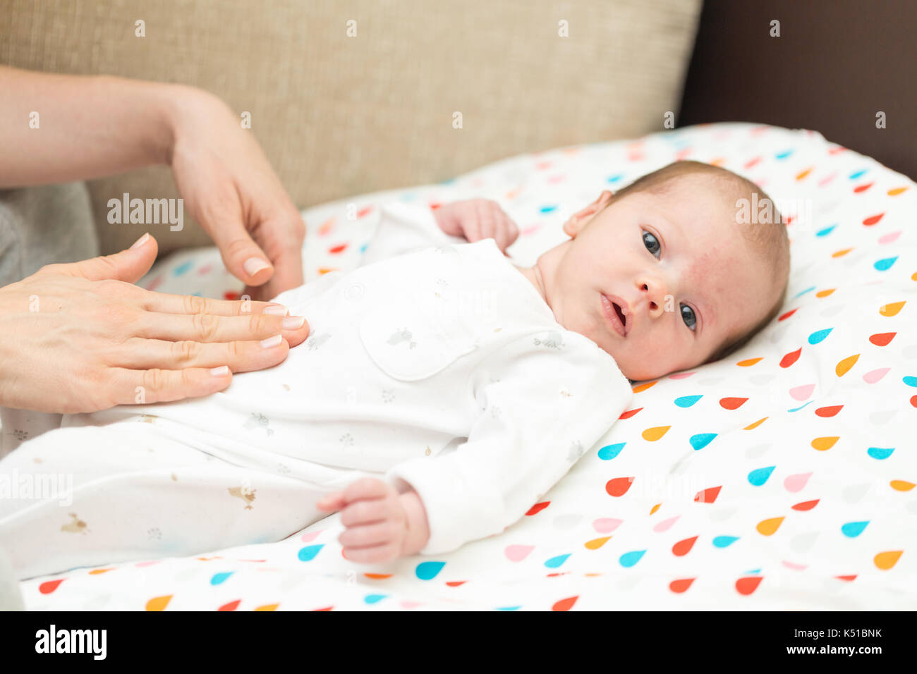 Newborn baby dressed in white laying on her back, with colics; mother's ...